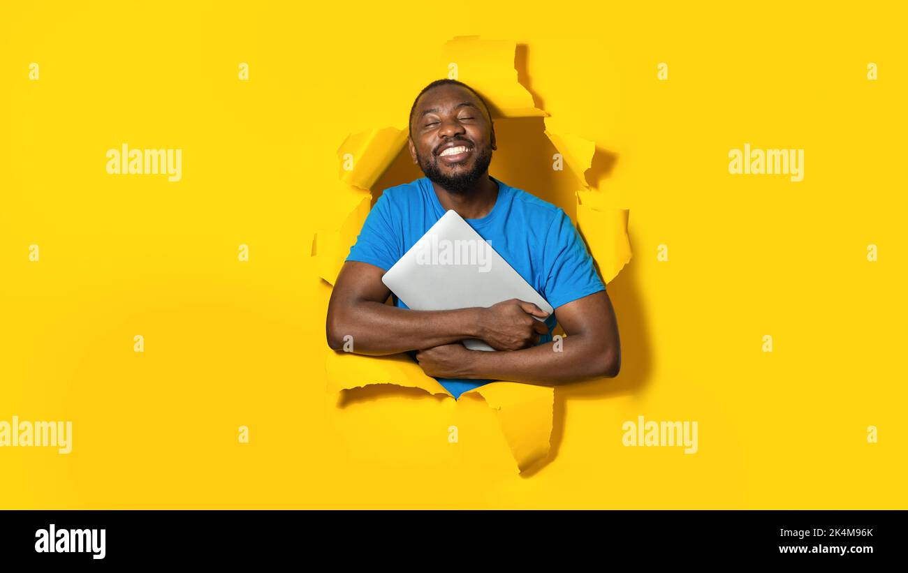 Gadget lover. Happy black man hugging laptop computer and smiling ...