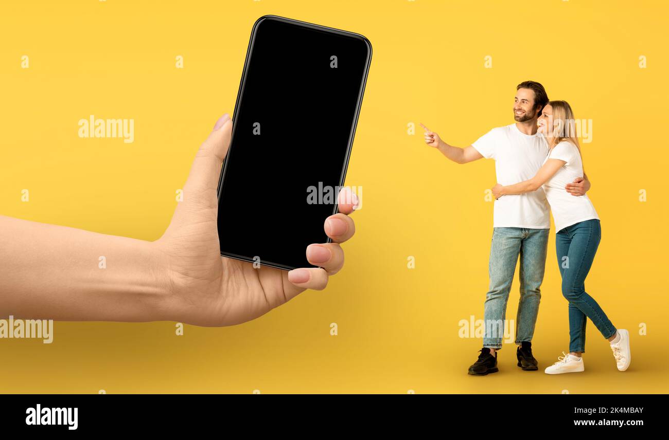 Smiling young european male hugging female and pointing finger at huge ...