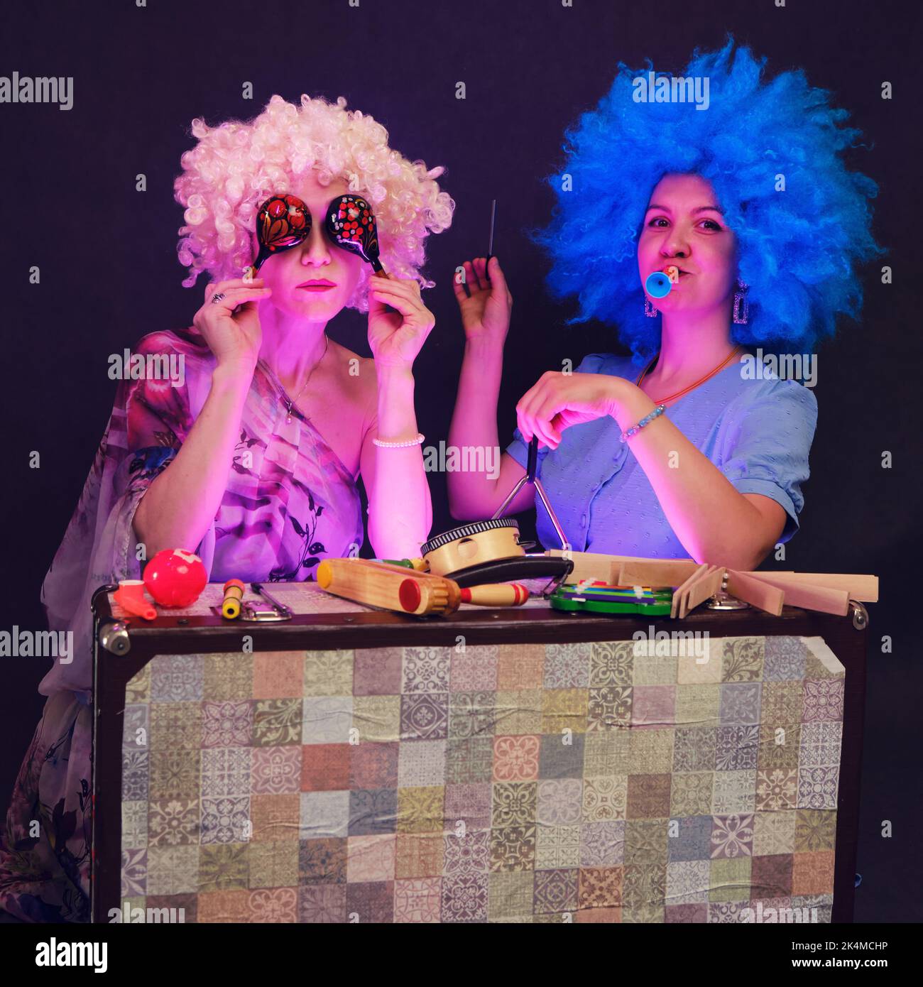 Happy women in funny wigs give a musical performance on a studio black ...