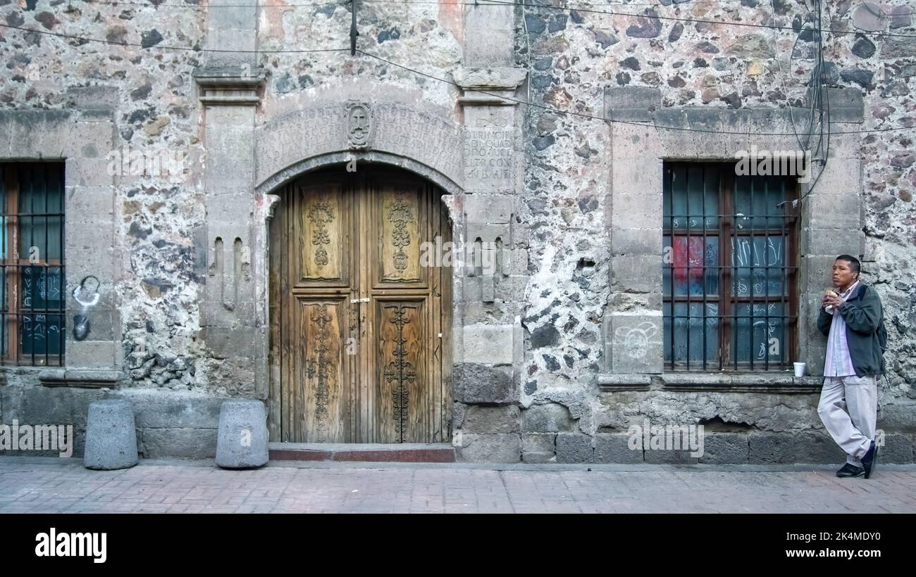 man eating on the facade of a building with wood and stone door, mexico ...
