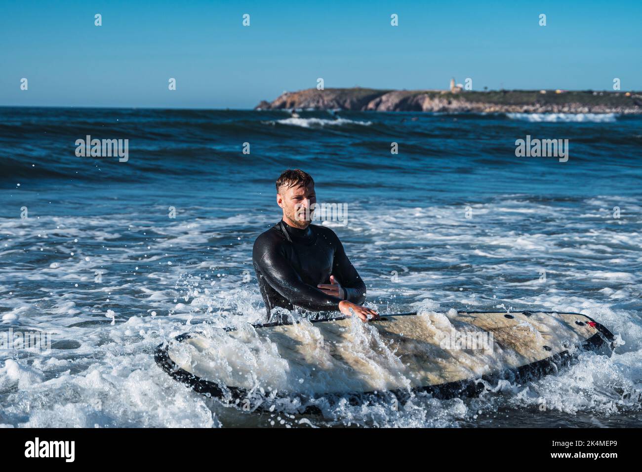 Man holding his surfboard on the shore, while fighting against the ...