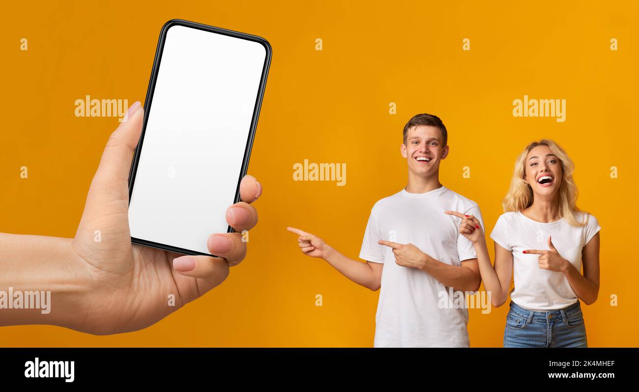 Laughing young european man and woman point fingers at huge smartphone ...