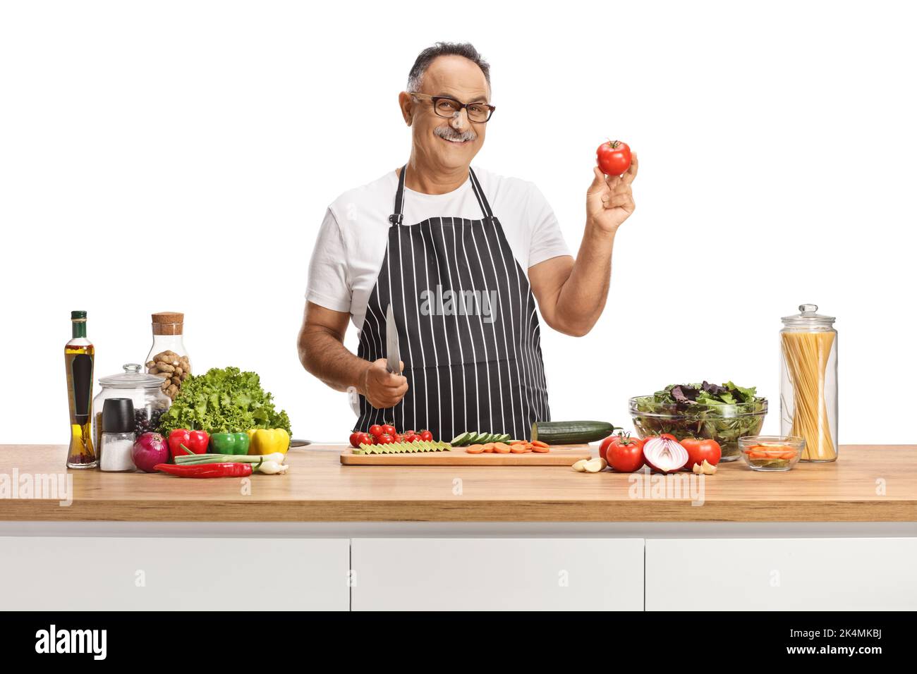 Mature man behind a kitchen counter holding a knife and a tomato ...