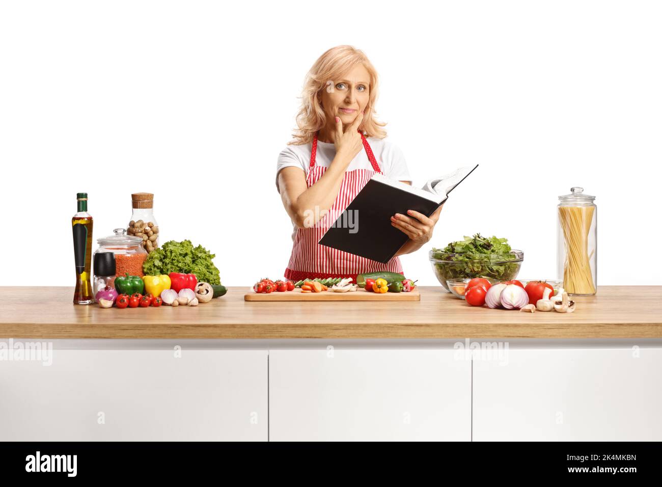 Woman behind a kitchen counter holding a cook book and thinking what to ...