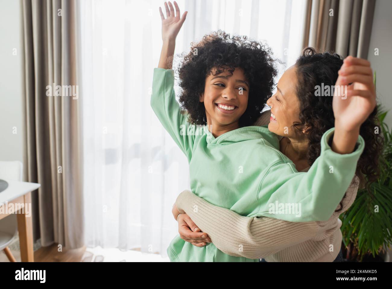 cheerful african american woman hugging happy preteen daughter with raised hands,stock image ...