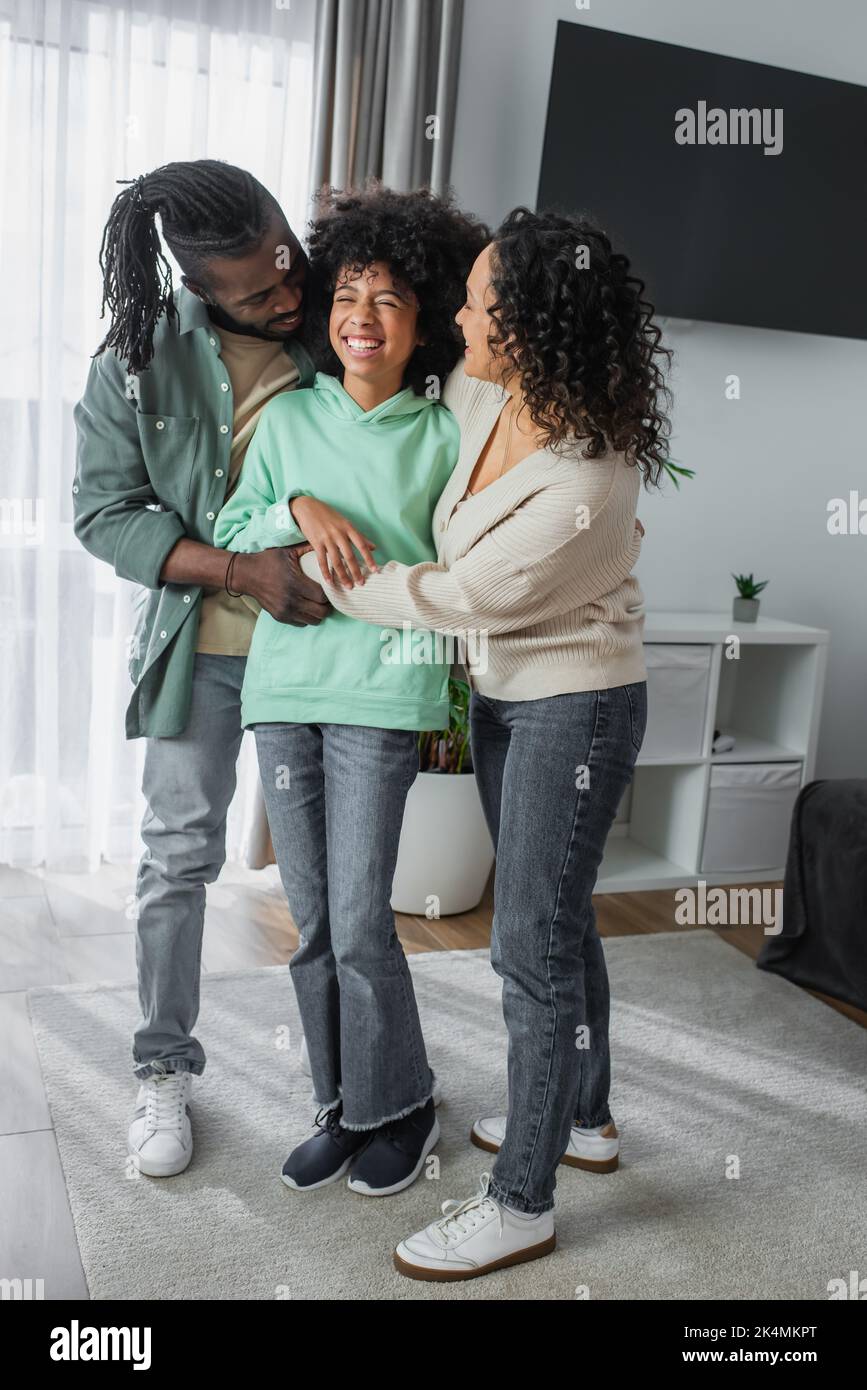 full length of happy african american parents hugging cheerful preteen ...