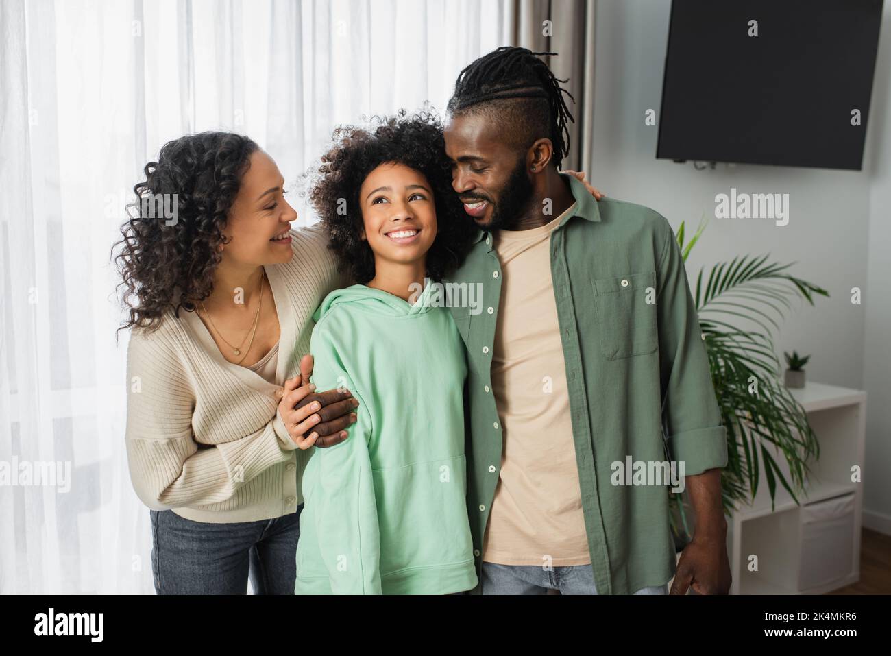 happy african american parents hugging cheerful and curly daughter at ...
