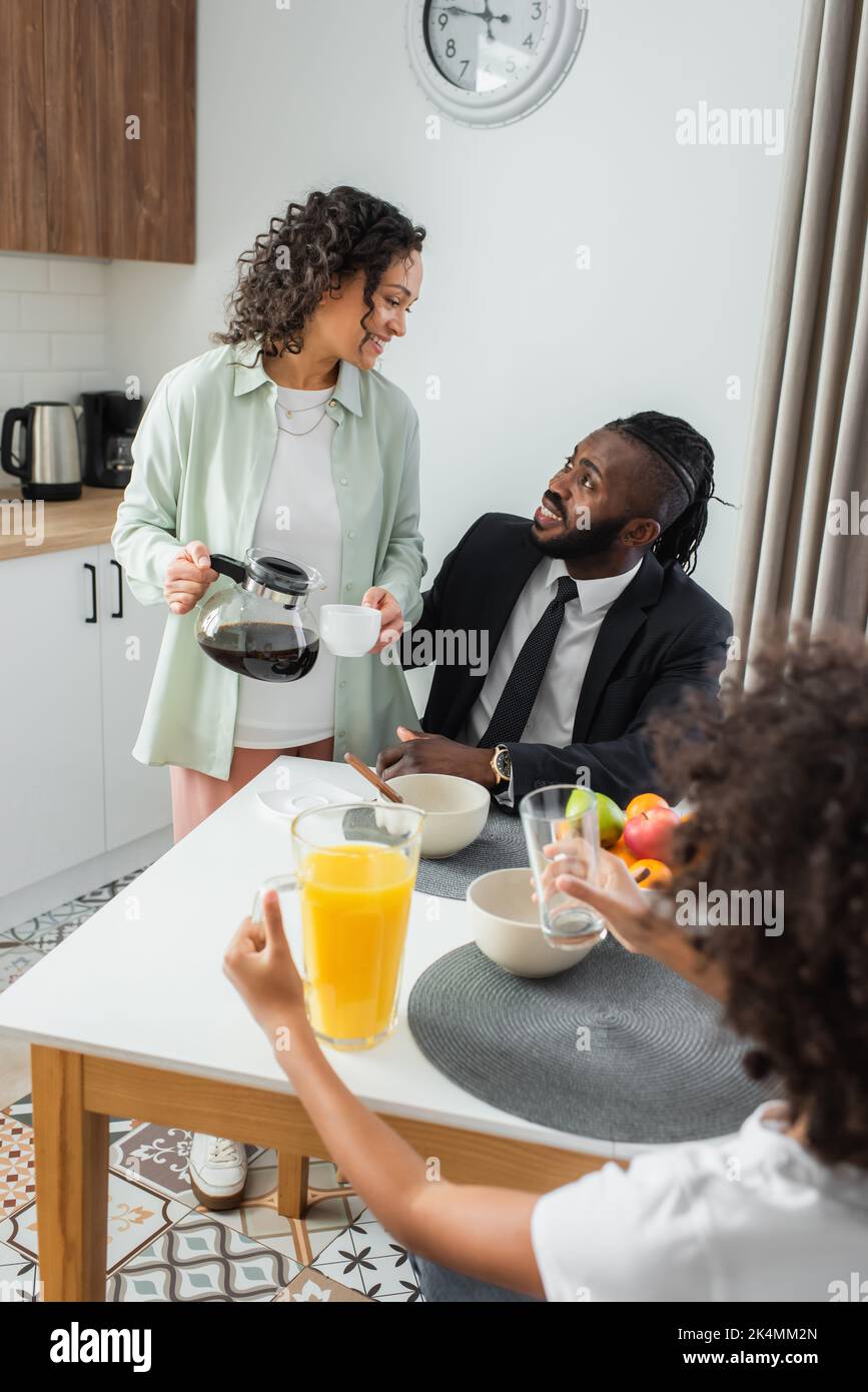 happy african american woman holding coffee pot and cup while looking ...