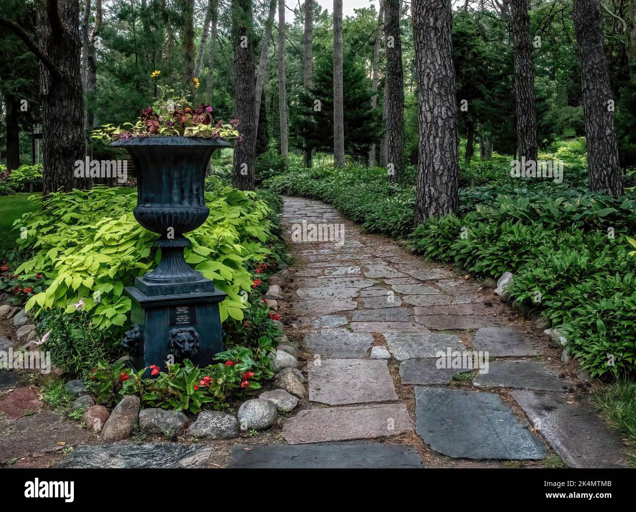 Antique planter filled with flowers along a stone path with plants and ...