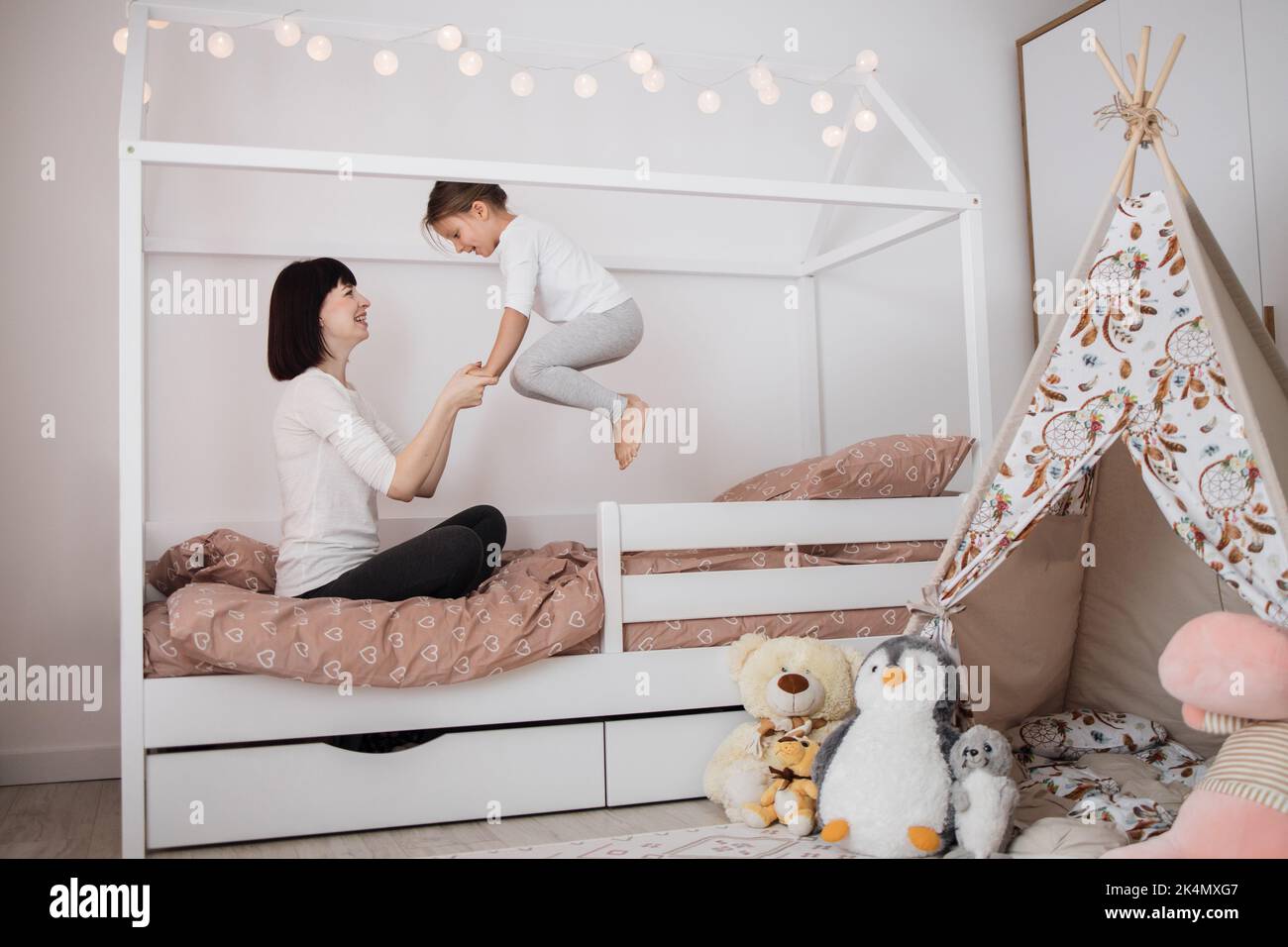 Cheerful mum babysitter play with cute active small kid girl jump on ...