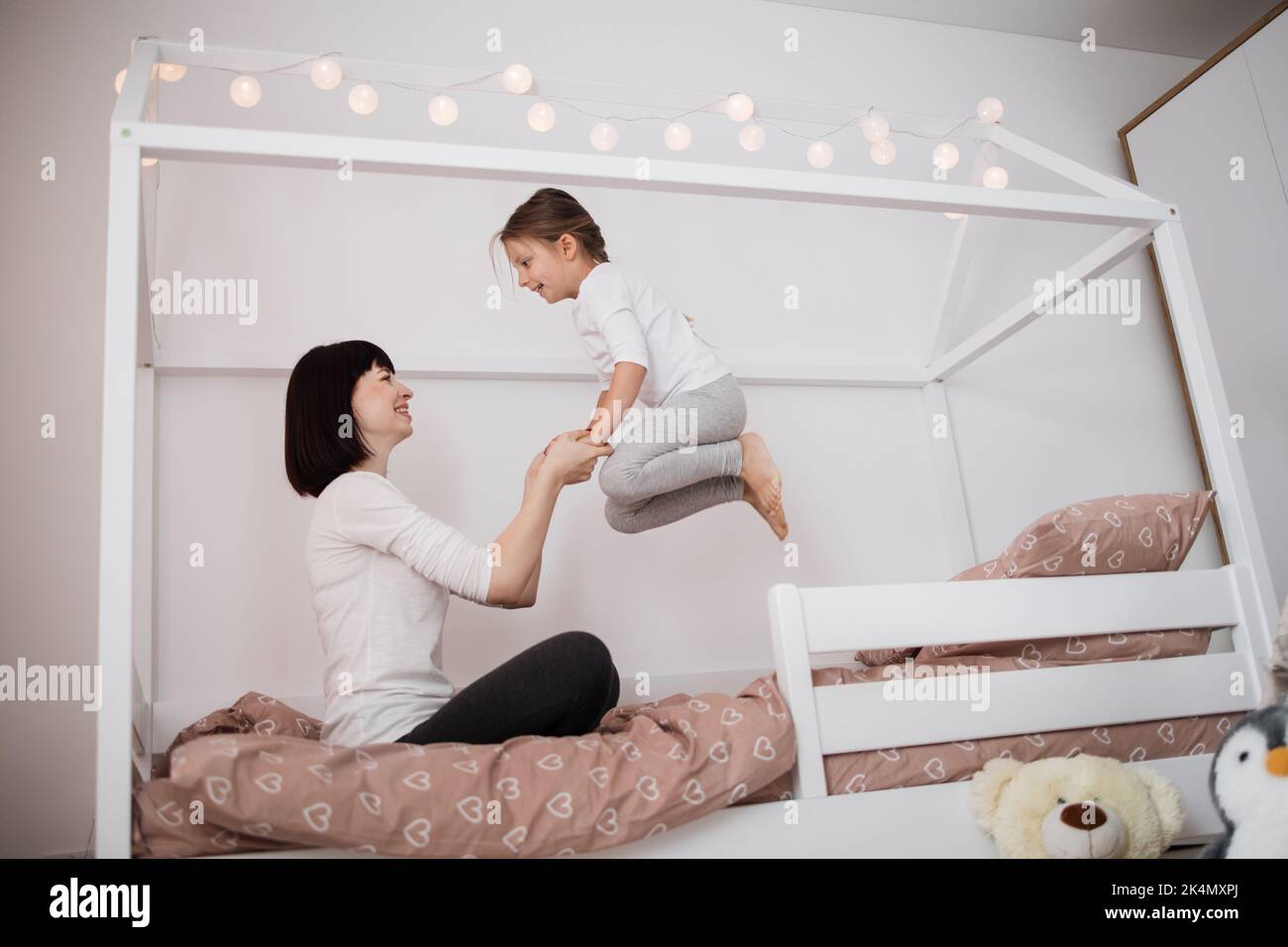 Cheerful mum babysitter play with cute active small kid girl jump on ...