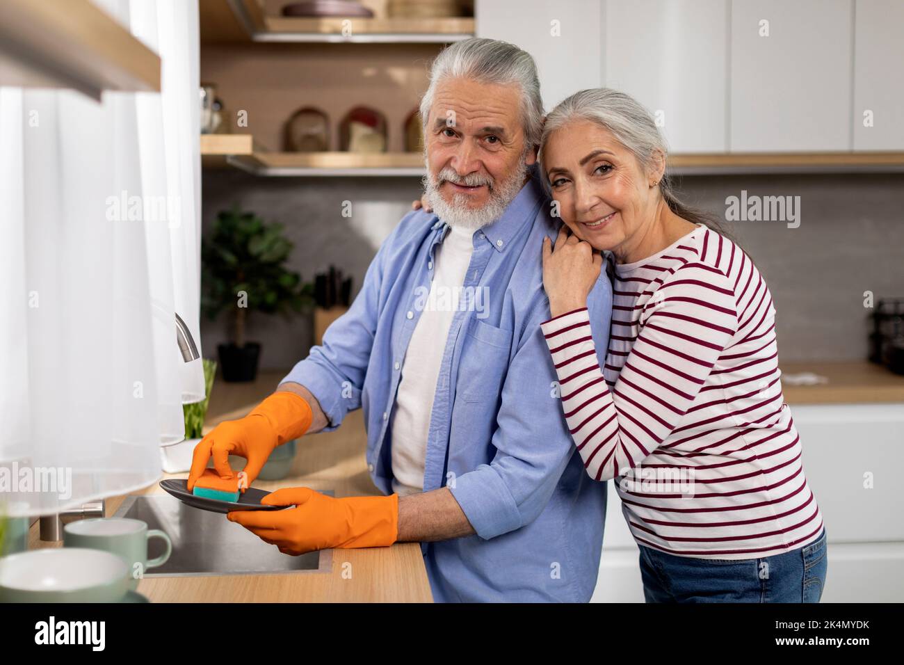Happy senior couple washing dishes in kitchen while doing cleaning at ...