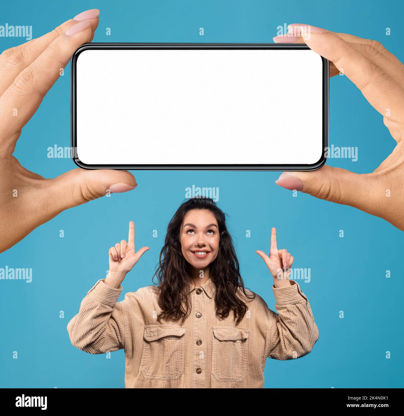 Happy inspired young european woman pointing fingers at huge smartphone ...
