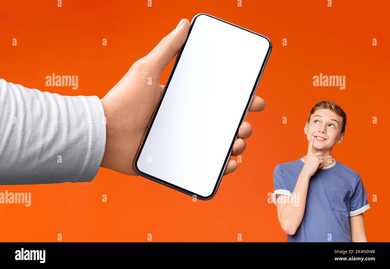Smiling pensive teenager caucasian boy looking at big smartphone with ...