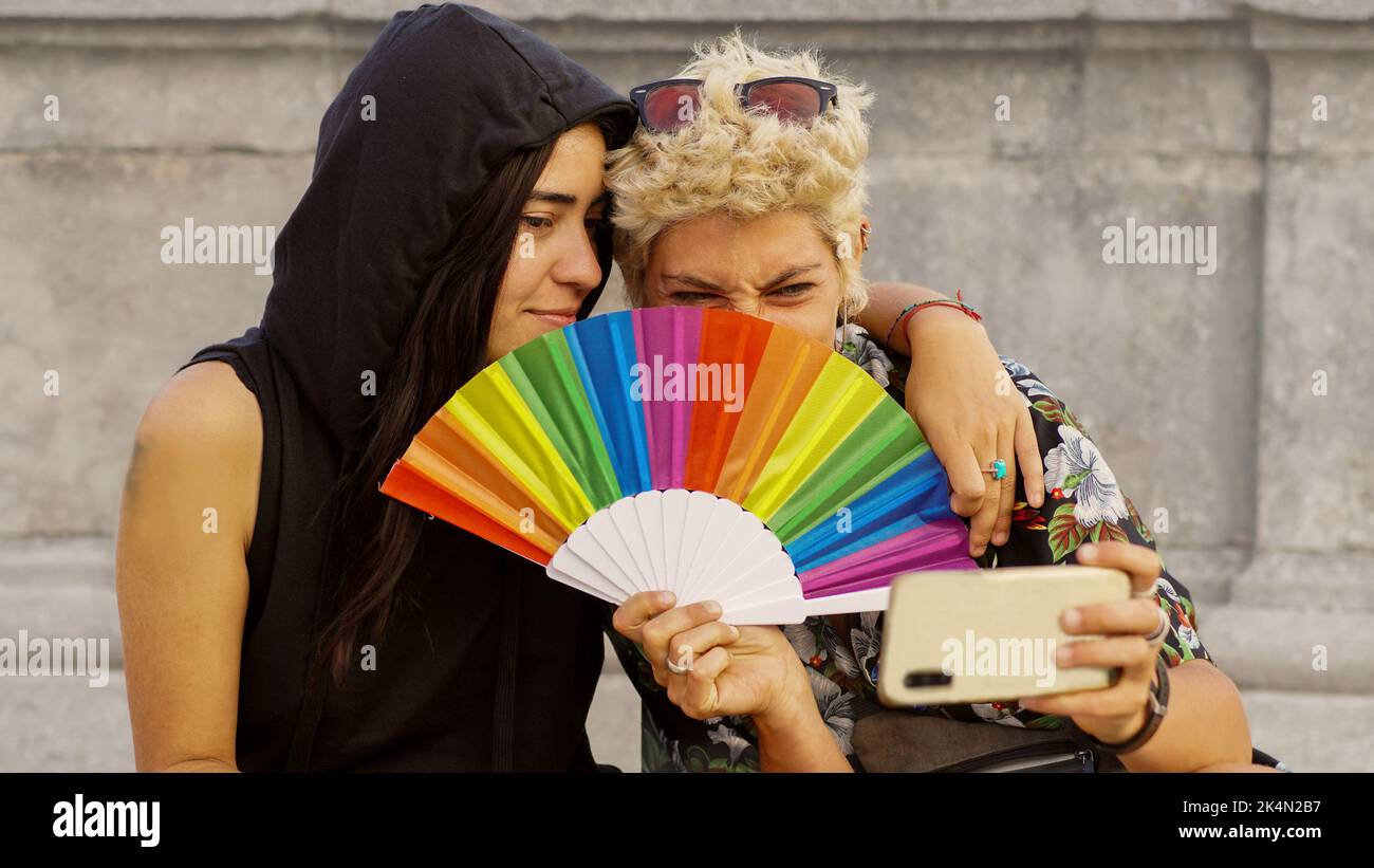 a non-binary couple with a rainbow fan and a mobile. Gay Pride's day ...