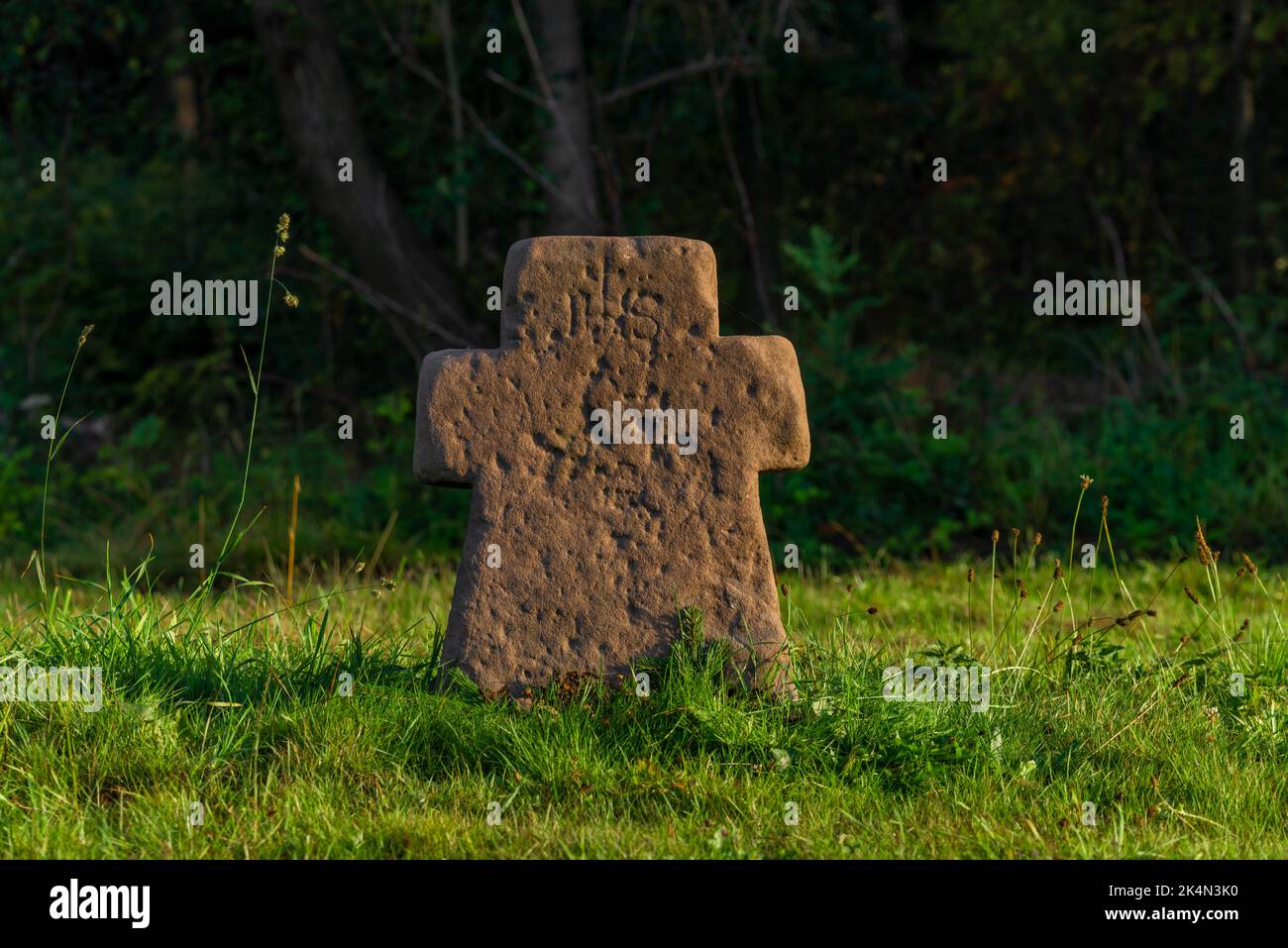 Very old stone crucifix on green meadow near dark forest near Krkonose ...