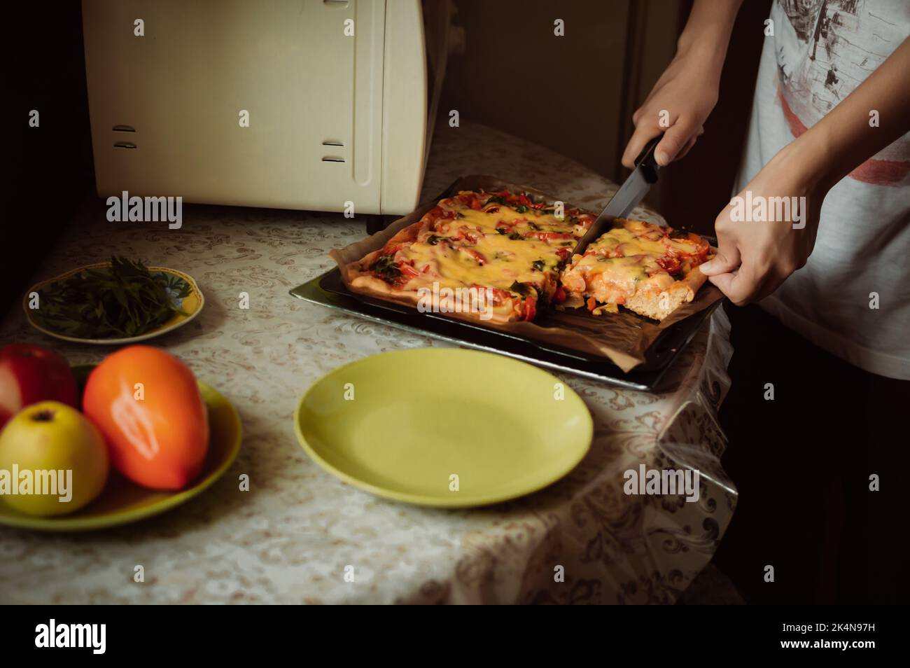 Girl cuts homemade pizza on baking sheet on kitchen table Stock Photo ...