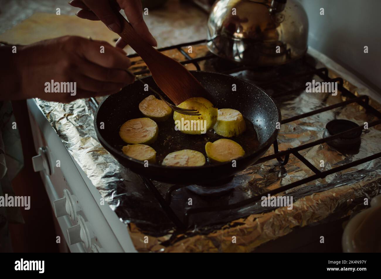 Hands turn over zucchini in flour in frying pan on gas stove Stock ...