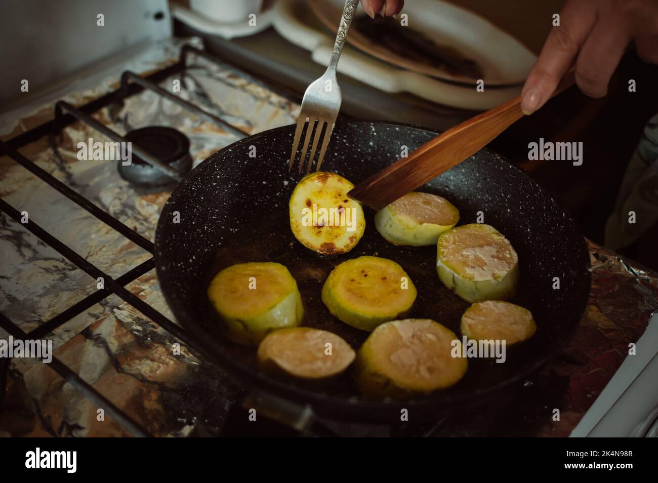 Hands turn over zucchini in flour in frying pan on gas stove Stock ...