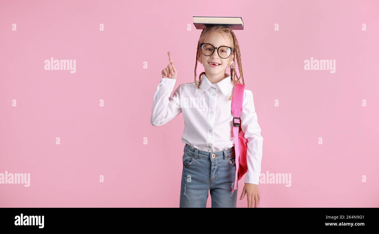 Little smiling girl in glasses with the book on her head is pointing ...