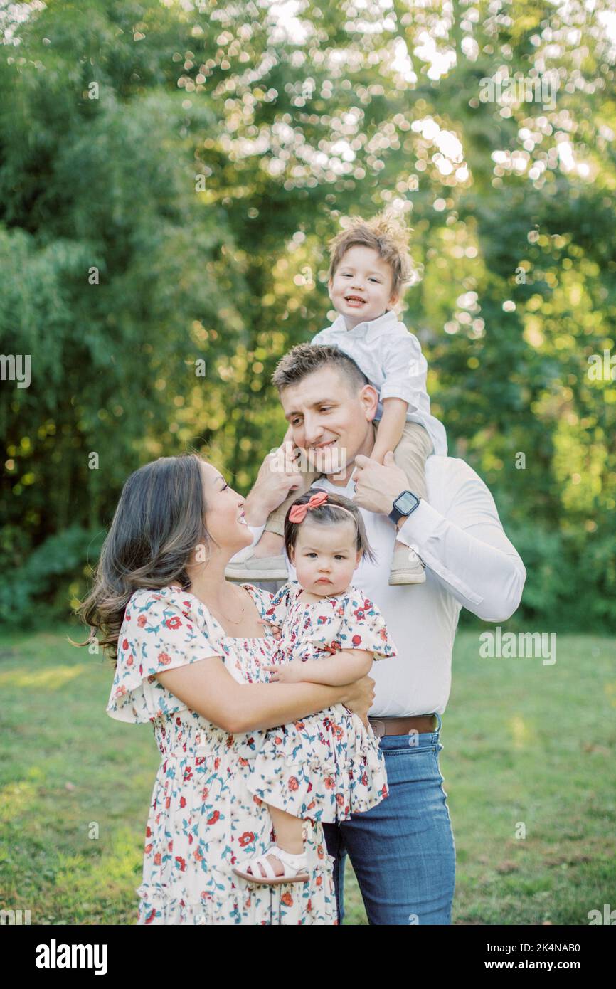 Multiracial parents hold their two toddlers while smiling together ...