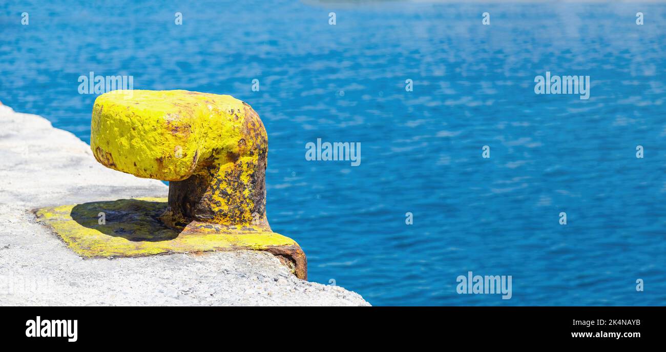 Yellow rusty port bollard on harbor pier, blur sea water background ...