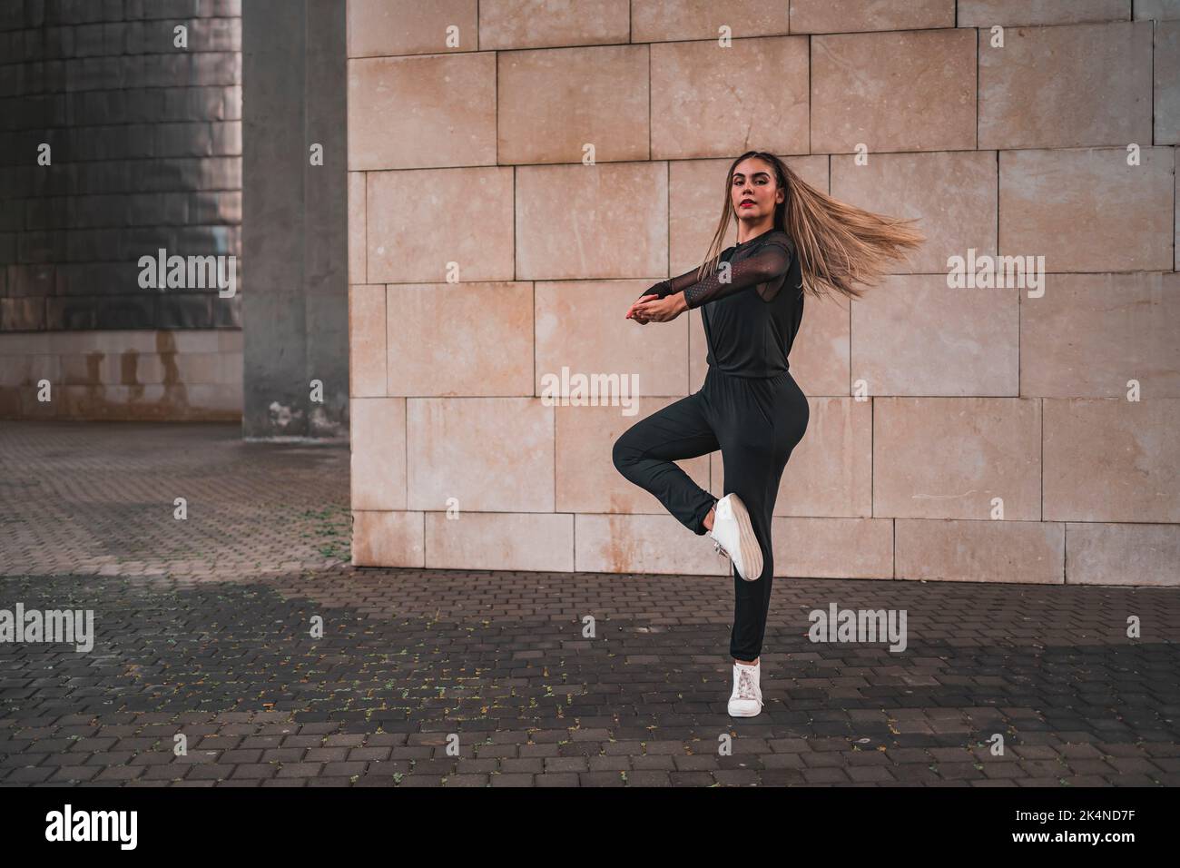 A young ballerina in a black suit does ballet pirouettes on the street ...