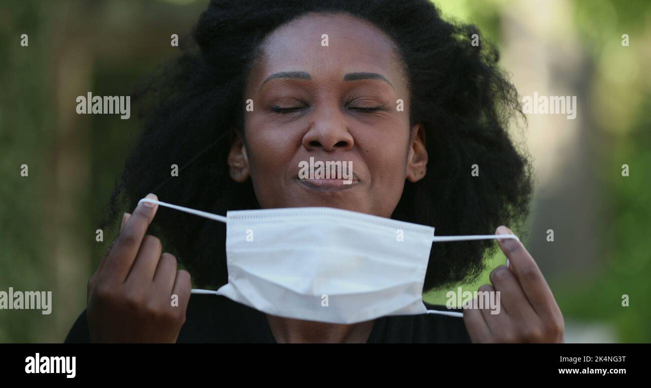 African woman taking off covid face mask feeling relief Stock Photo - Alamy