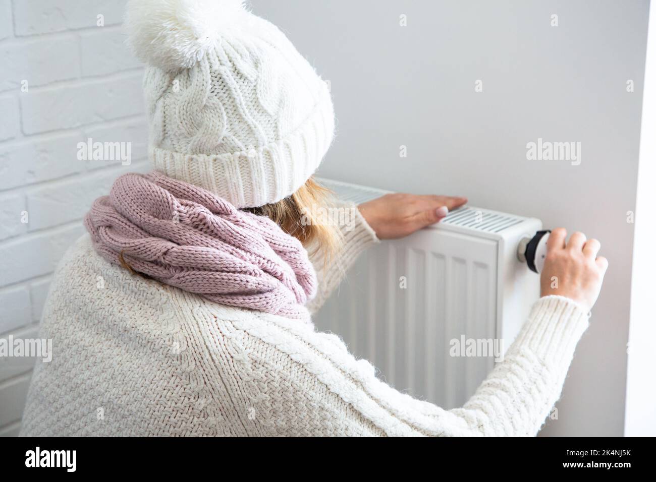 A woman in warm clothes near the radiator regulates the heat with a ...