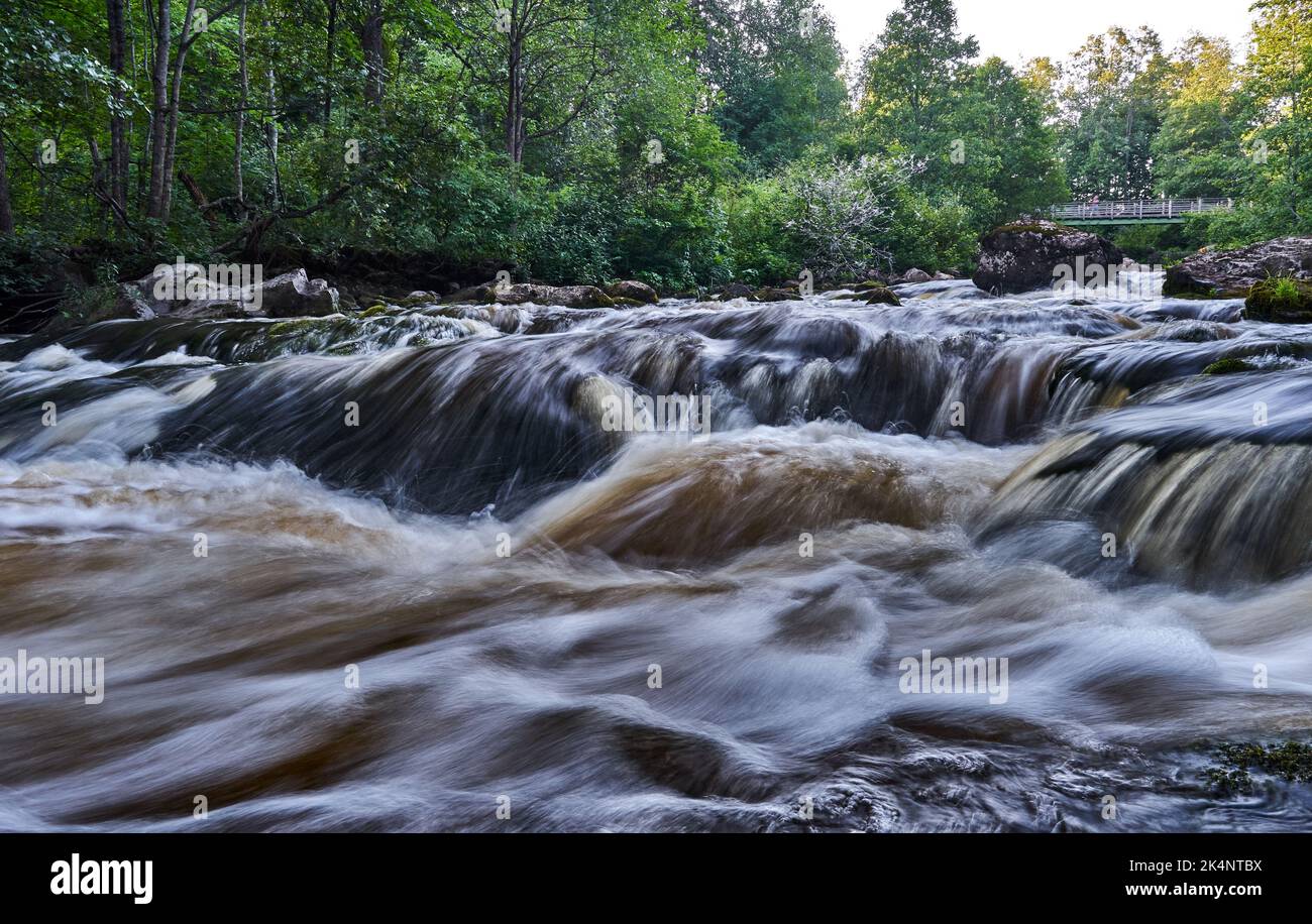 A long exposure shot of a waterfall flowing over rocks in a forest with ...