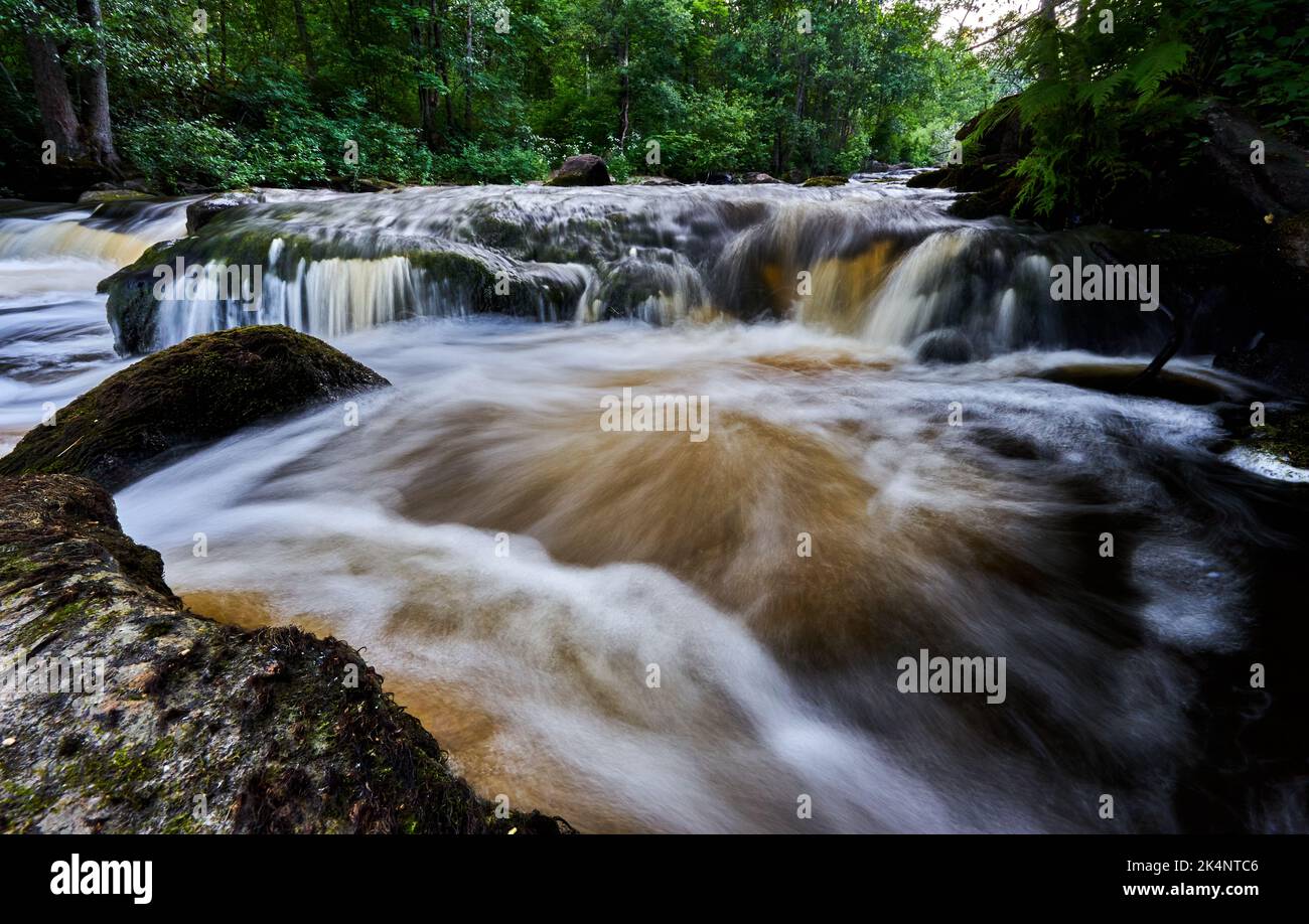 A long exposure shot of a waterfall flowing over rocks in a forest with ...