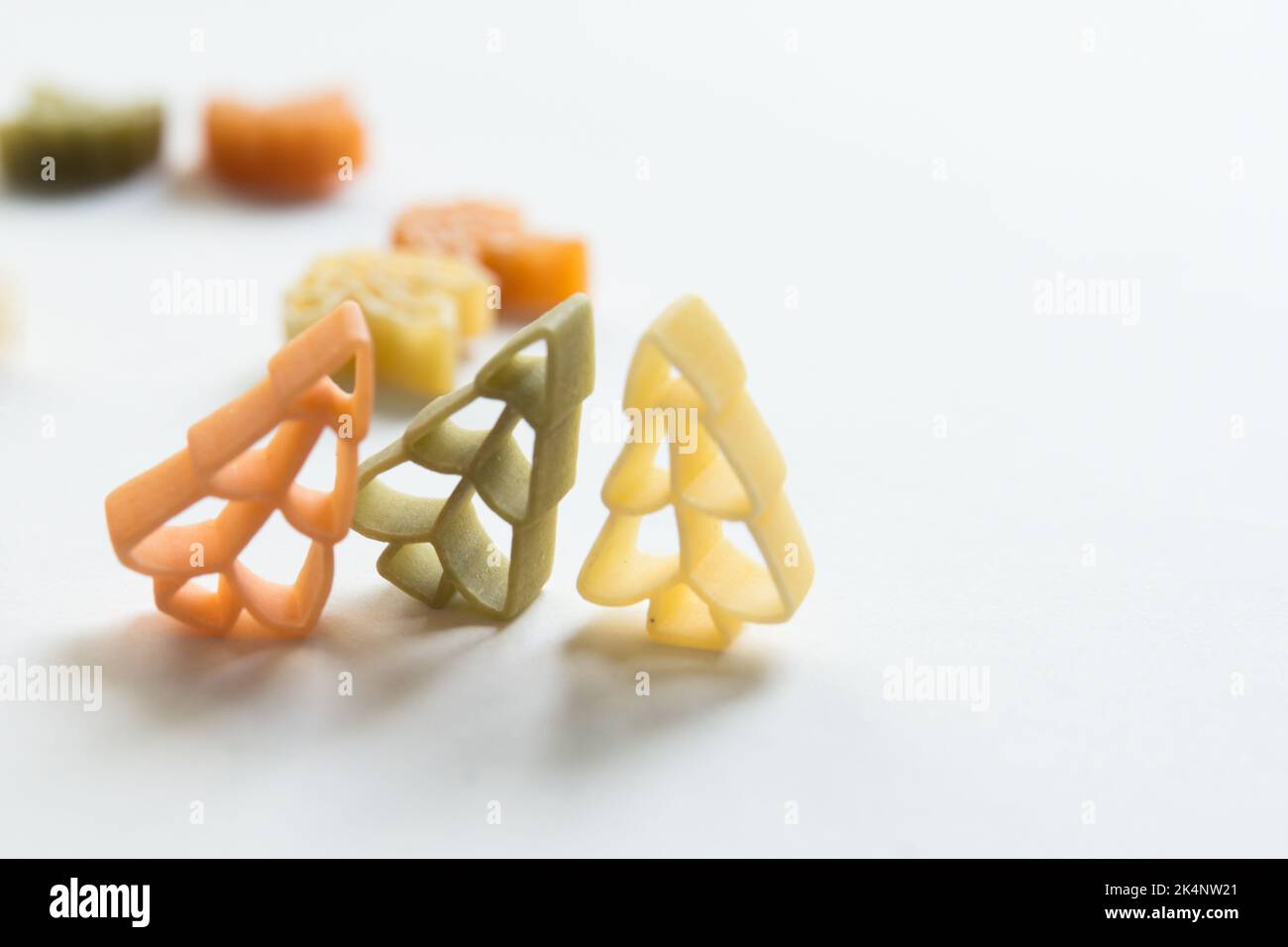 Raw pasta with cute shapes. Green, yellow and orange trees. White ...