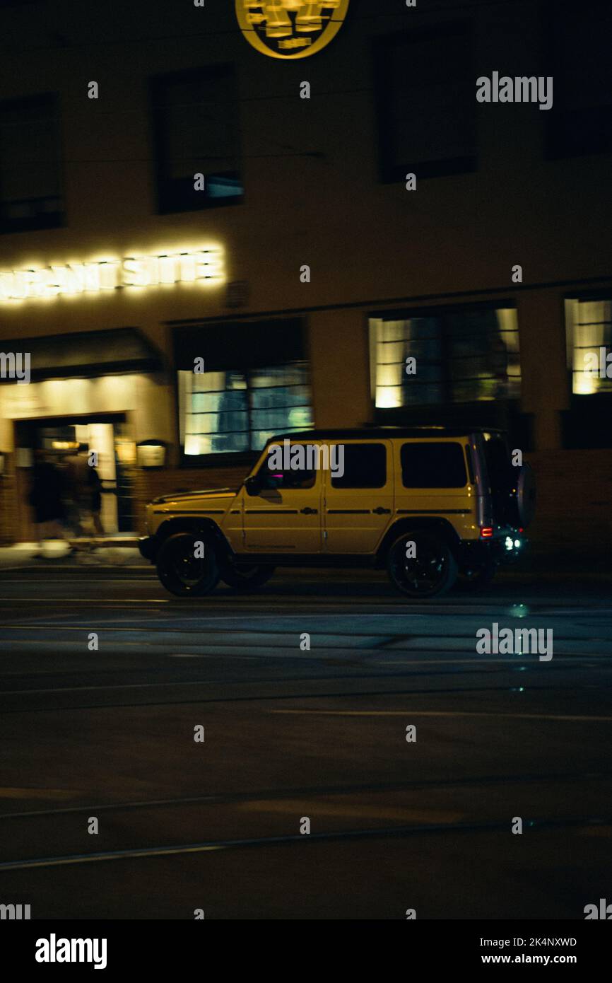 A vertical shot of a yellow Mercedes G Wagon driving on a road at night ...