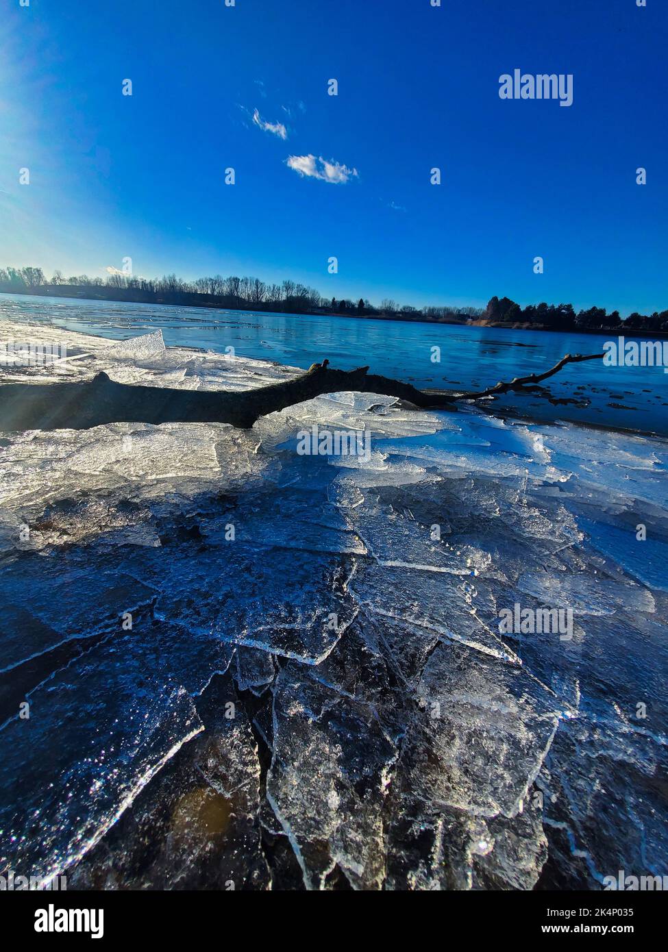 A vertical shot of cracked ice on a lake in winter with blue sky above ...
