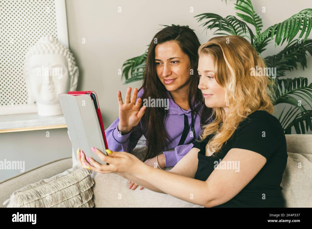 Two girls are sitting on the couch at home and making a video call to ...