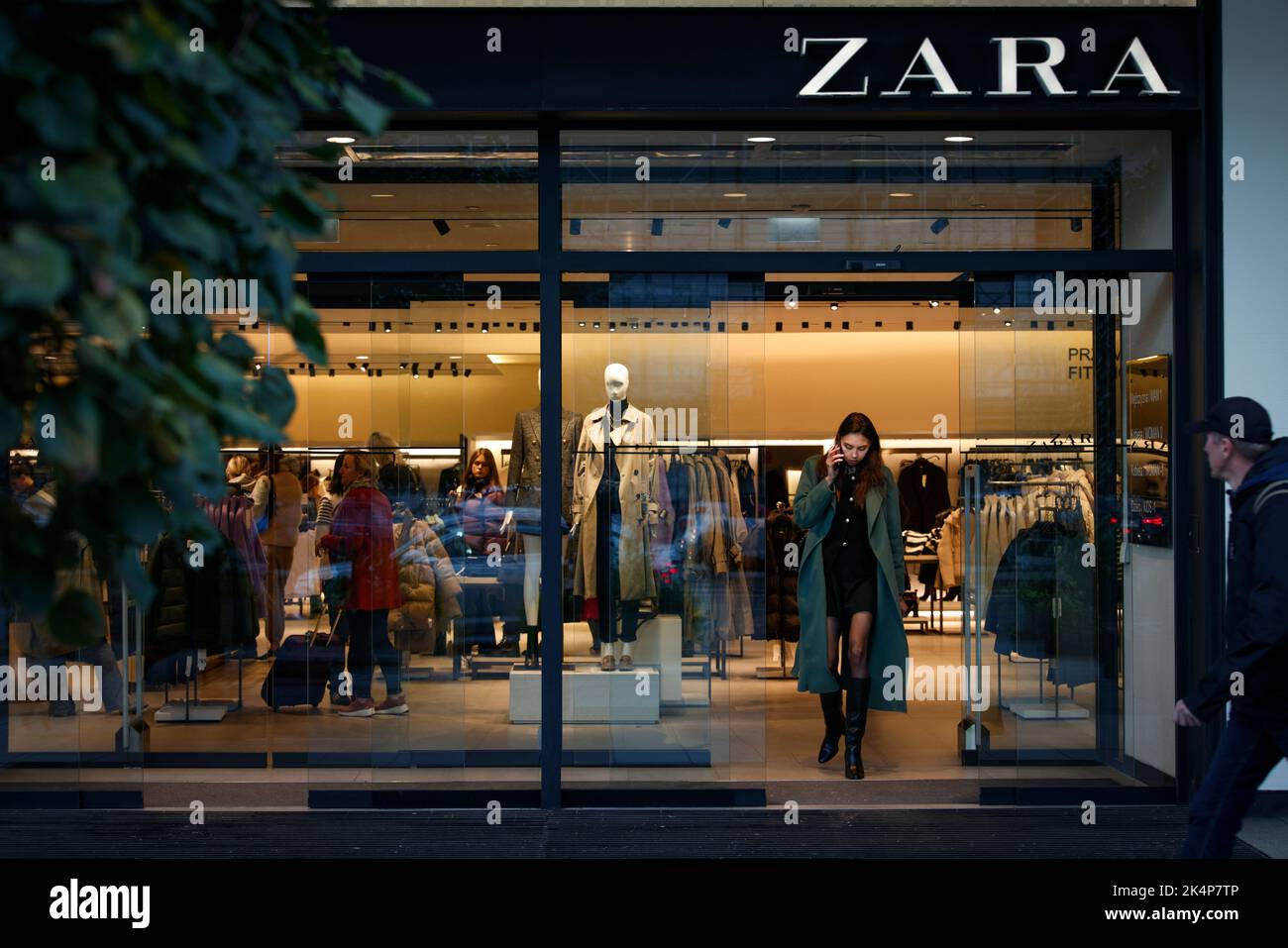 A woman in long boots and a long coat exits a Zara fashion shop in ...