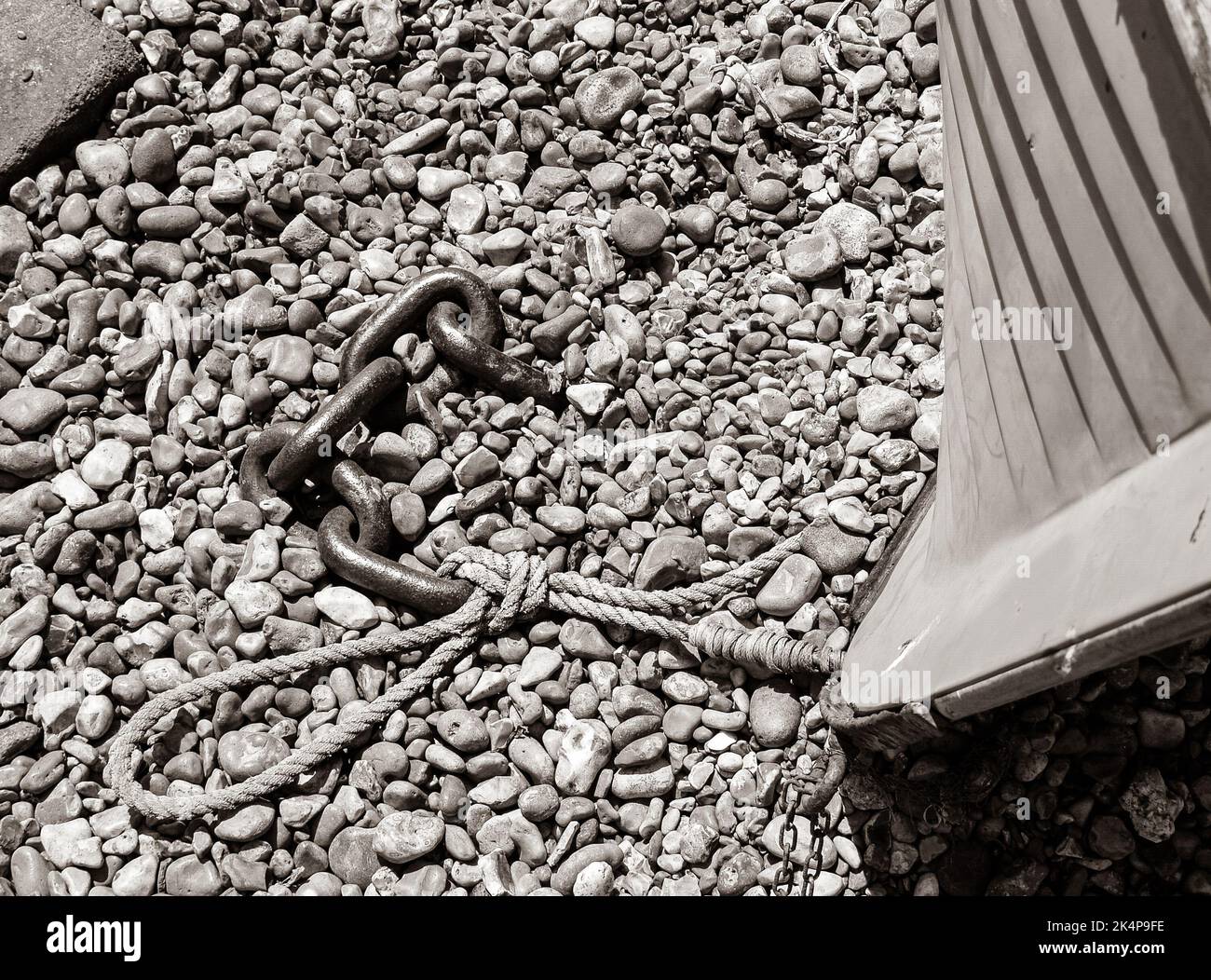Close-up blue dinghy on pebble beach secured by chain on Brighton Beach ...