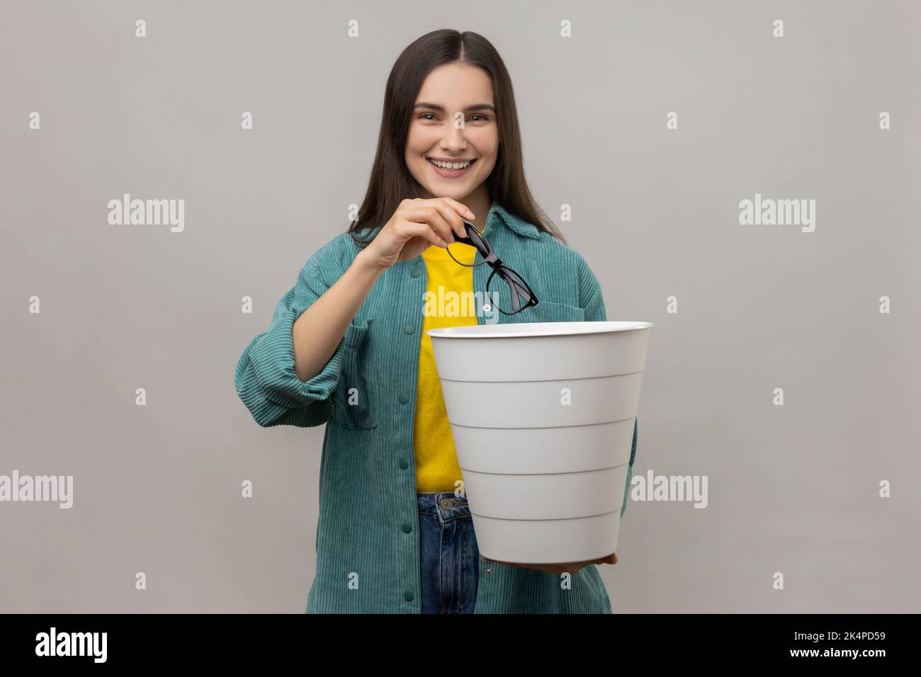 Smiling woman with dark hair standing holding trash bin and throwing ...