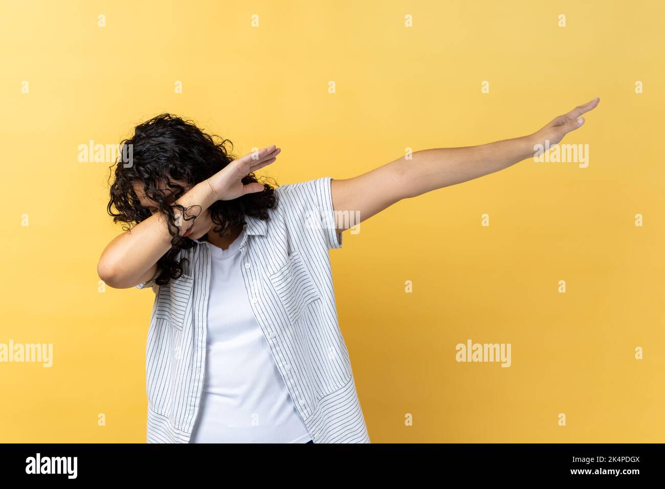 Portrait of young woman with dark wavy hair, hiding face with dab dance move, performing ...