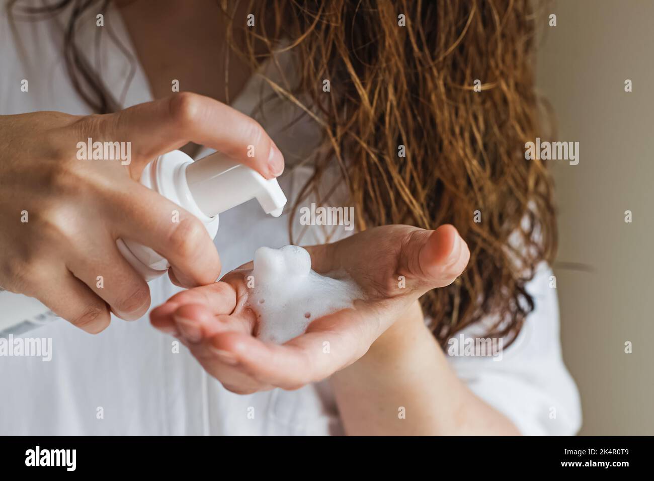 Woman's hand close-up with a styling white foam. Applying mousse for ...