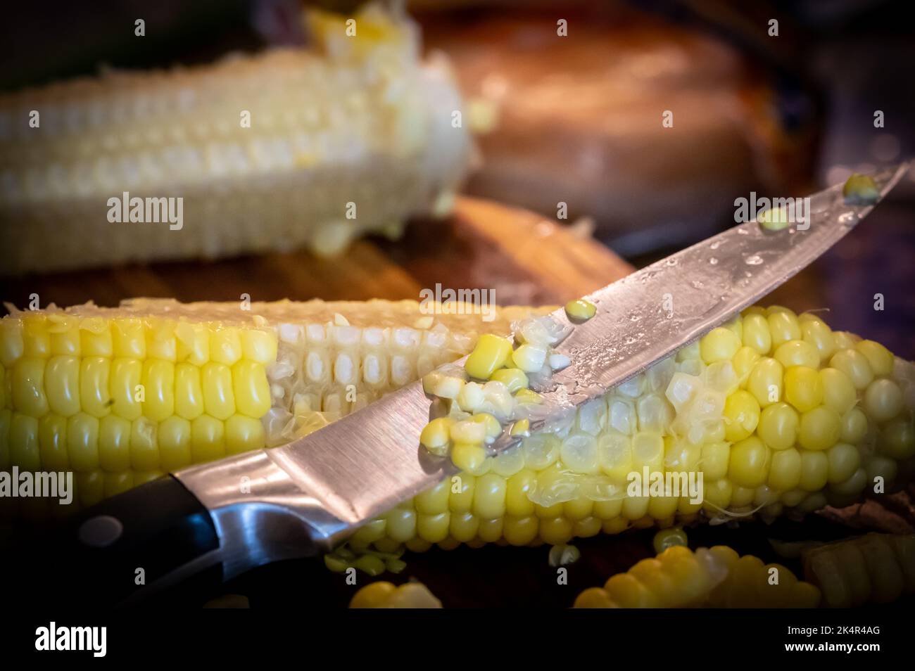 Using a knife to remove kernels from the cob of an ear of sweet corn ...