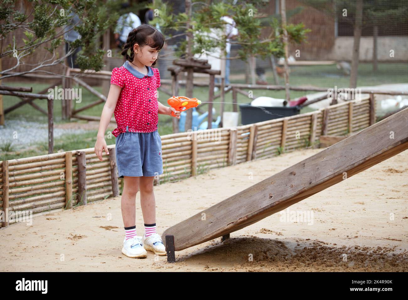 Little girl using water guns to spray wooden slider in the playground ...