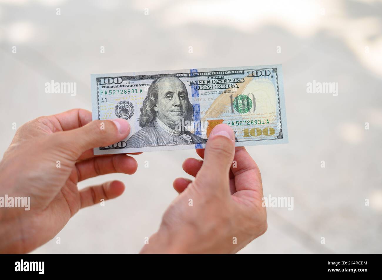 Close up 100 Dollar bank note in hand on grass background. One hundred ...