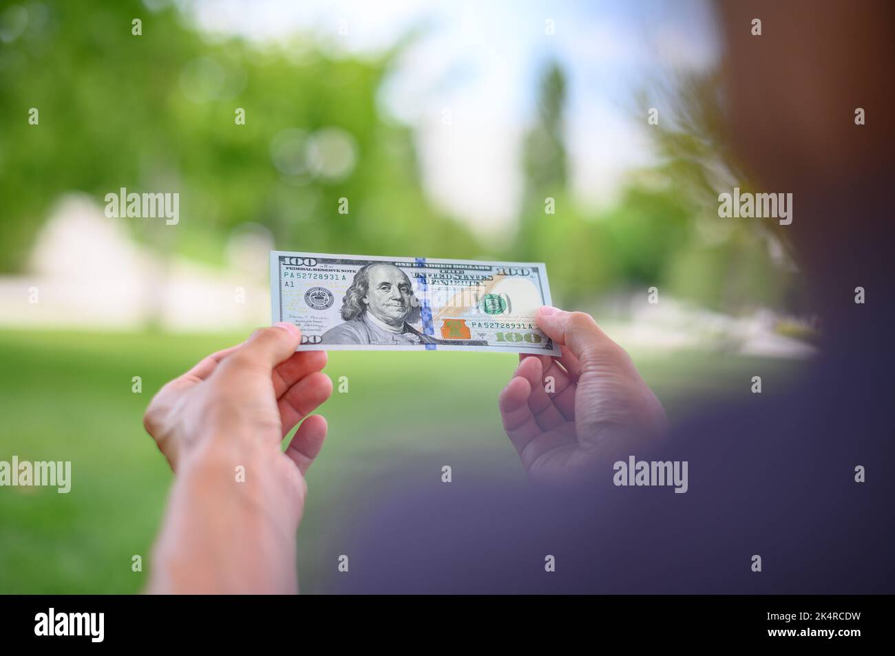 Close up 100 Dollar bank note in hand on grass background. One hundred ...