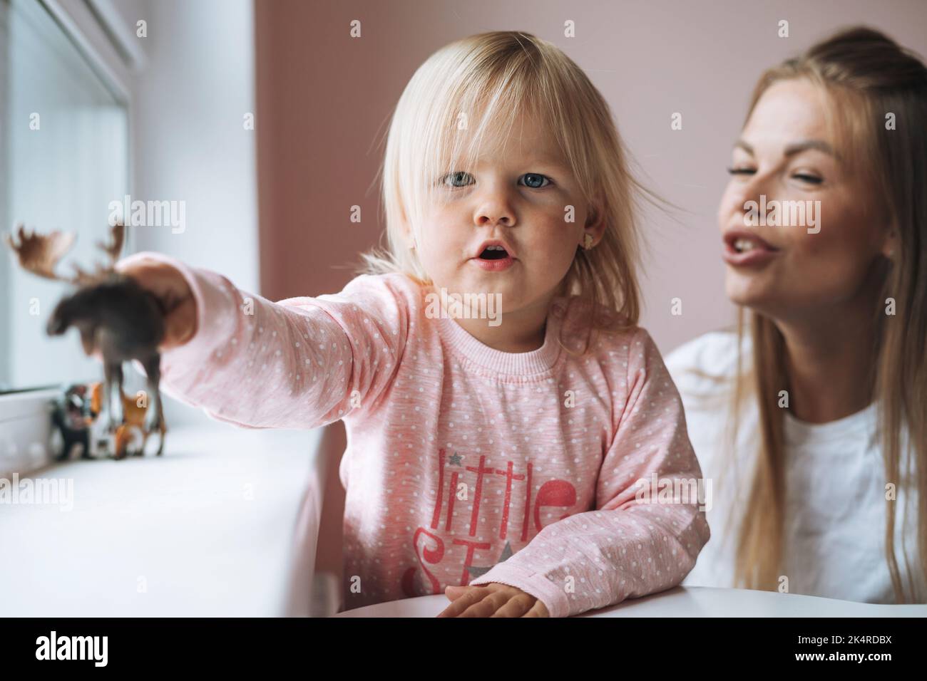 Little girl toddler with her mother playing with animal toys on window ...