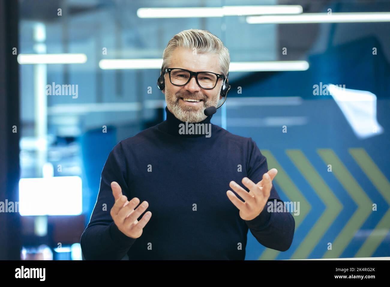 Online business training. A young handsome gray-haired man in headphones with a microphone ...