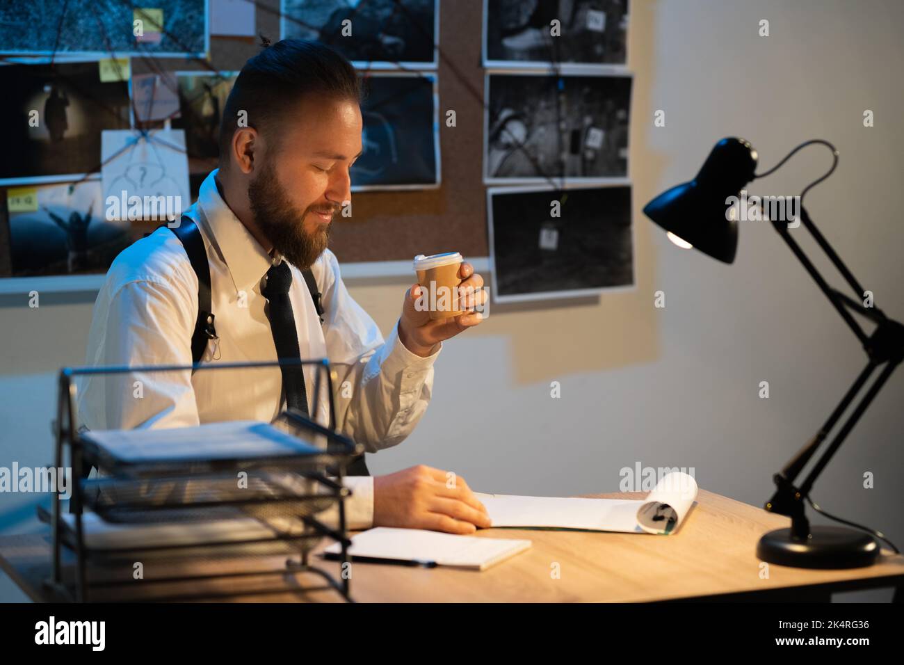 Detective working in the office at night drinking coffee, evidence ...