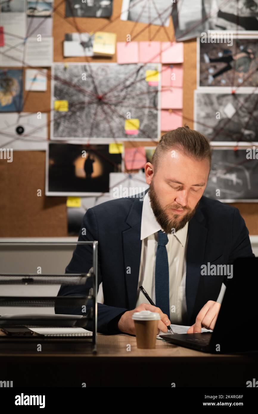 Professional detective sitting at table and writing in notebook ...