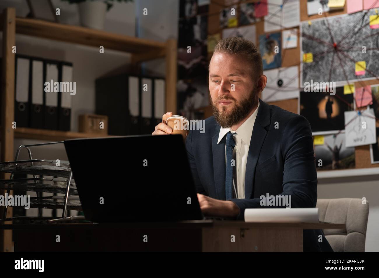 Detective working in office using computer at night, drinking coffee at ...