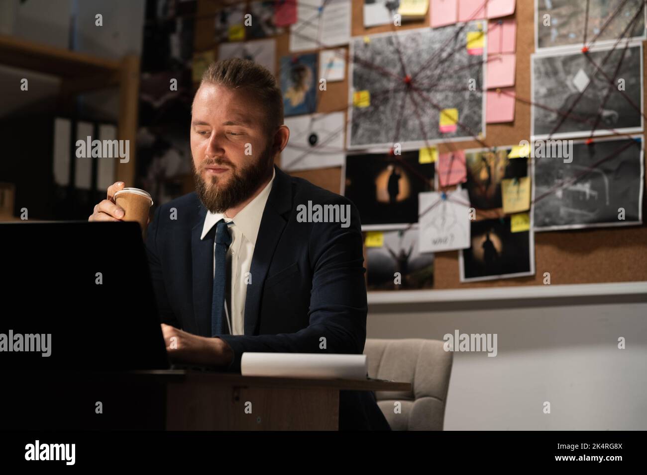 Detective working in office using computer at night, drinking coffee at ...